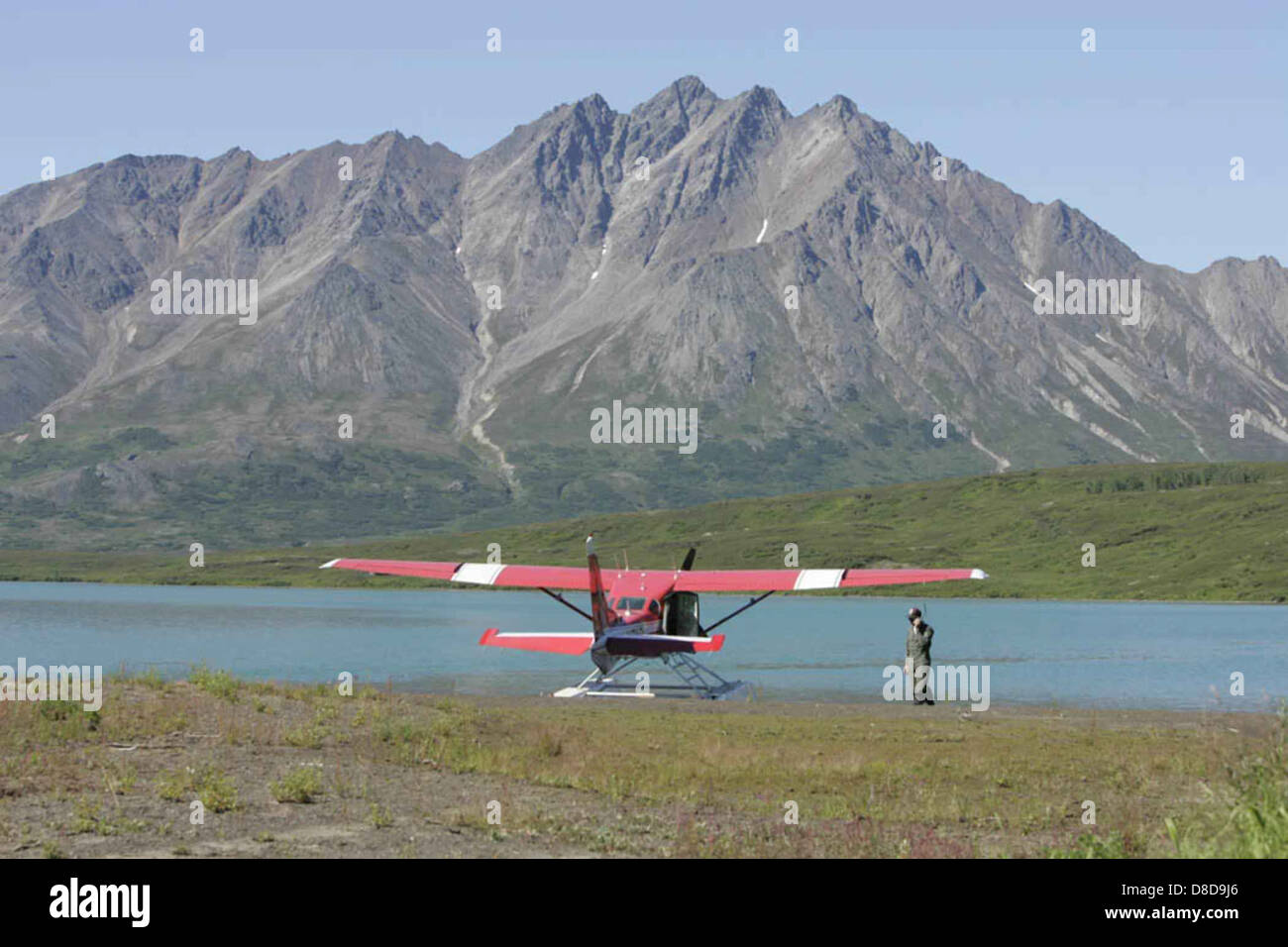 A small red water plane sits on the water, with a man standing next to ...