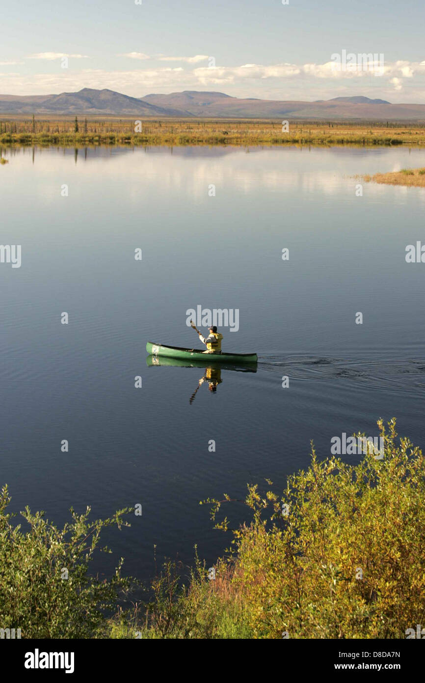 A solo canoer navigating calm waters with a paddle, surrounded by ...
