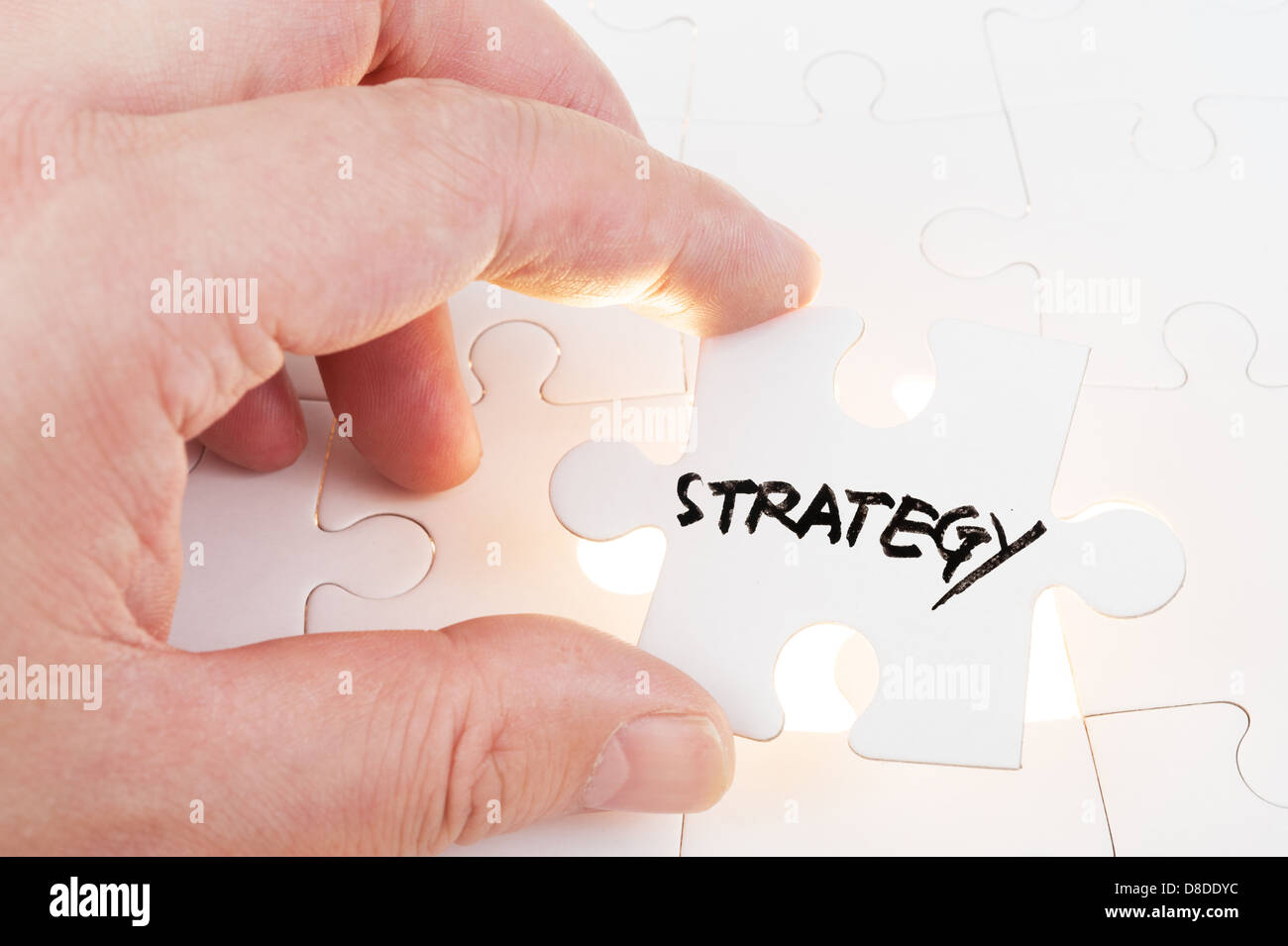 Hand holding puzzle piece which written strategy word and inserting it ...