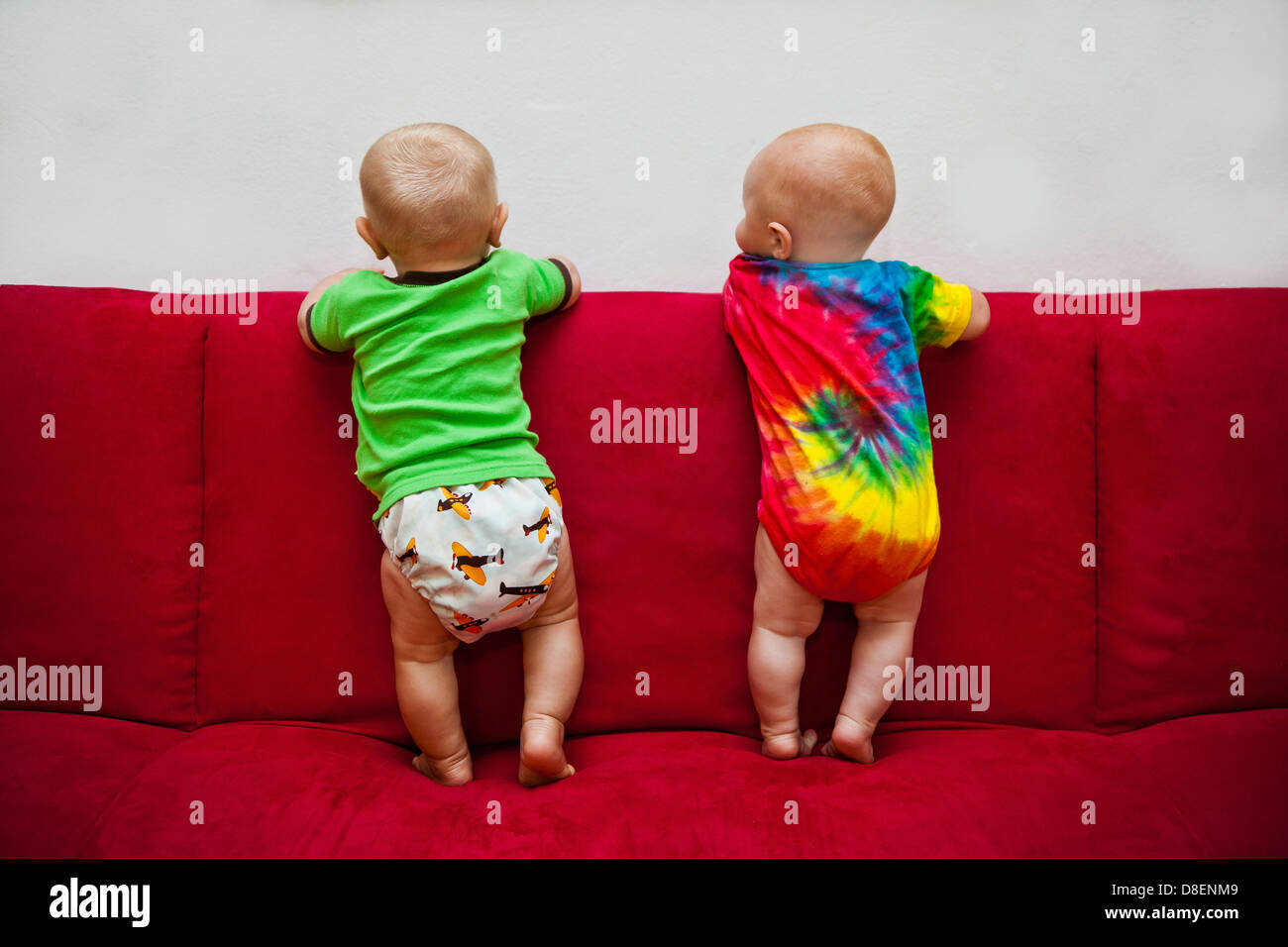Two babies standing on red sofa Stock Photo - Alamy