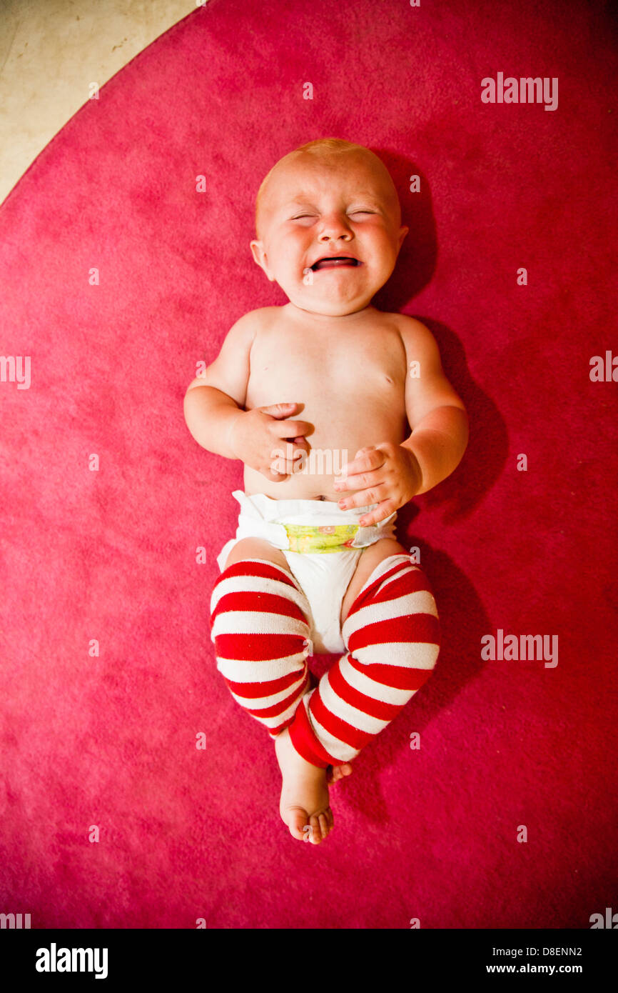 Crying baby on pink rug Stock Photo - Alamy
