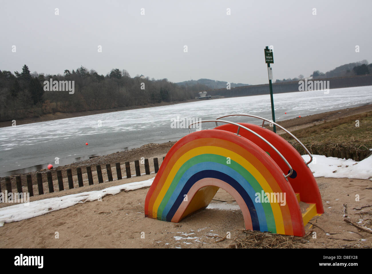 A rainbow coloured children's slide, contrasted against a dull frozen ...