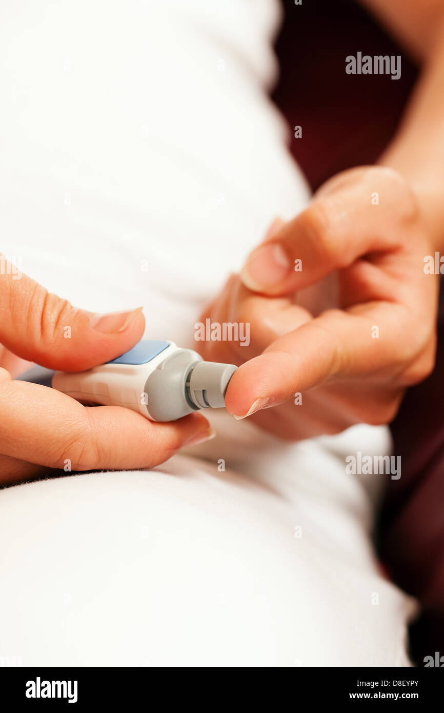 Woman taking a blood sample from her finger for a blood glucose level ...