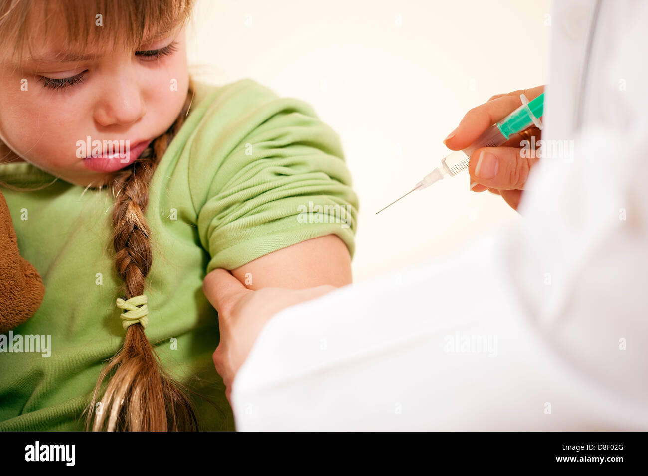 Doctor in his practice with syringe and a little girl child, she is ...