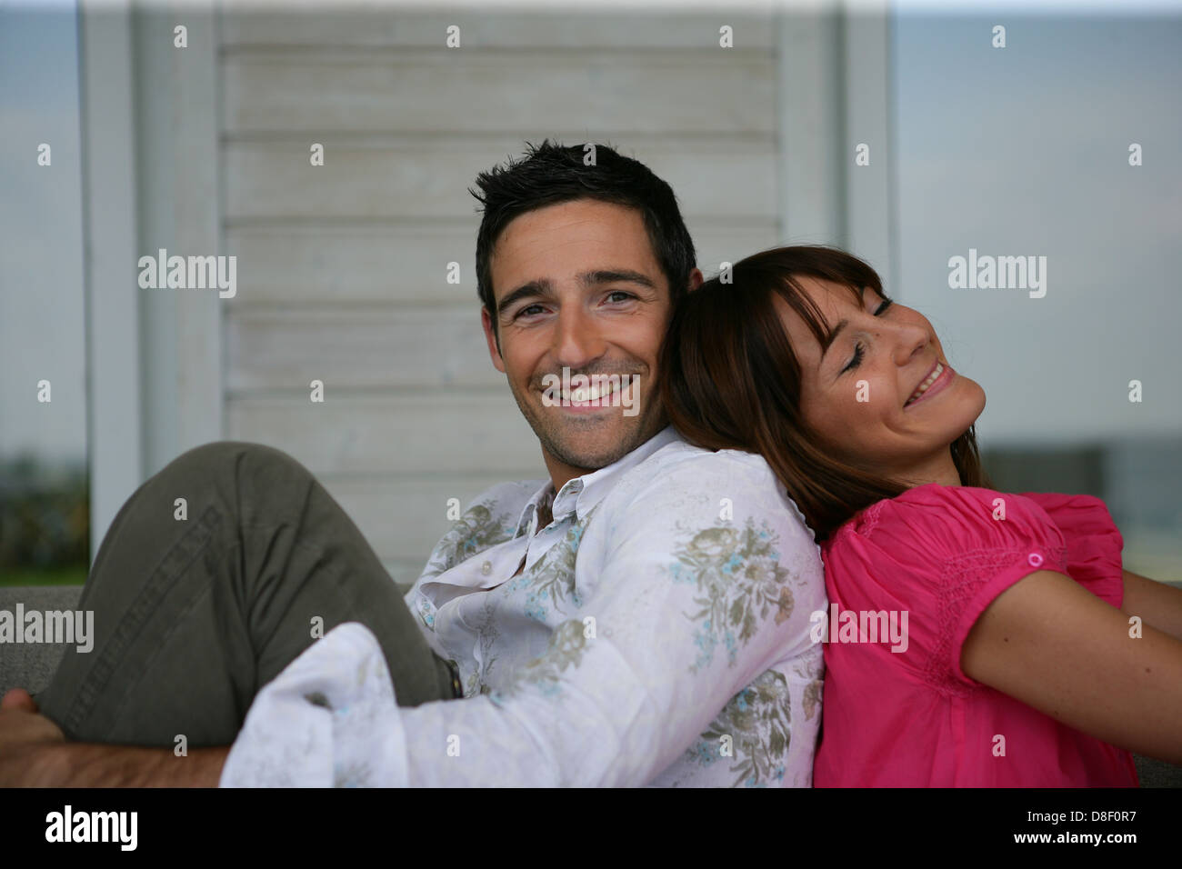 Couple sat back to back on porch Stock Photo - Alamy