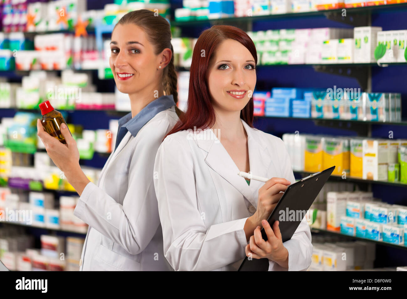 Pharmacist with female assistant in pharmacy standing in front of shelf ...