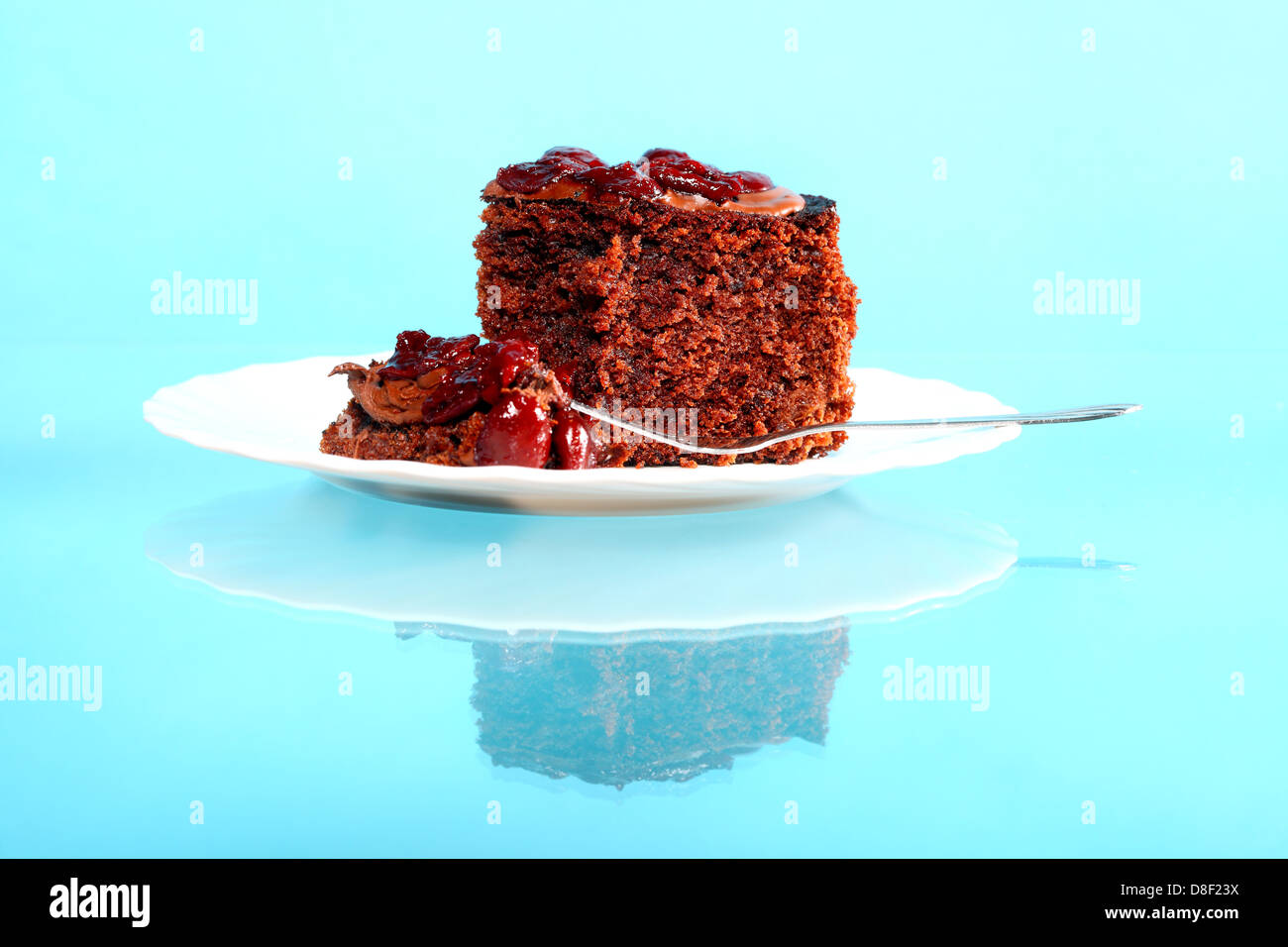 Piece of chocolate cake with icing and cherry on white plate blue ...