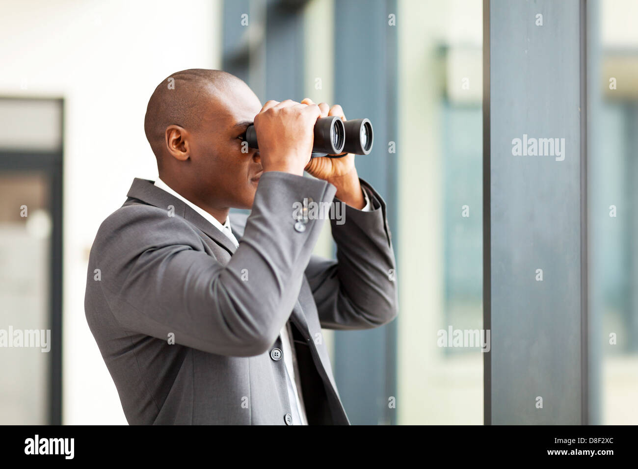 determined african american businessman using binoculars in office ...