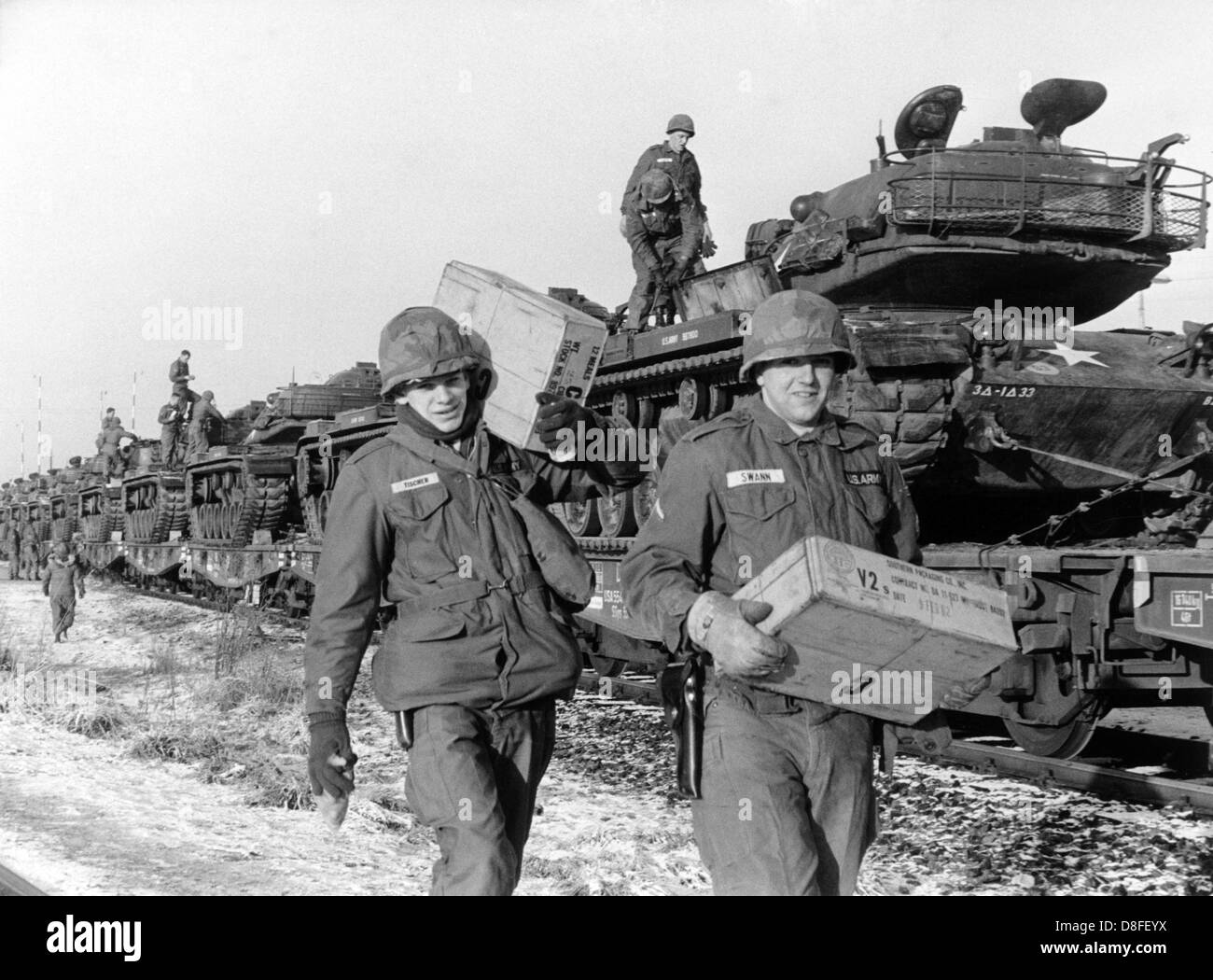 American soldiers carry boxes with equipment in front of US tanks ...