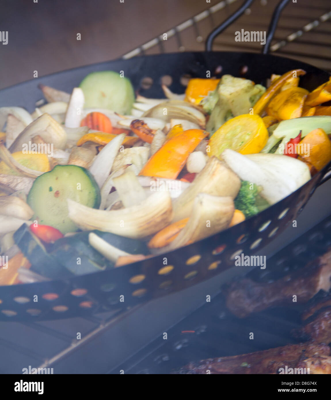 A grilling pan with vegetables in it, on a grill with meat showing on ...
