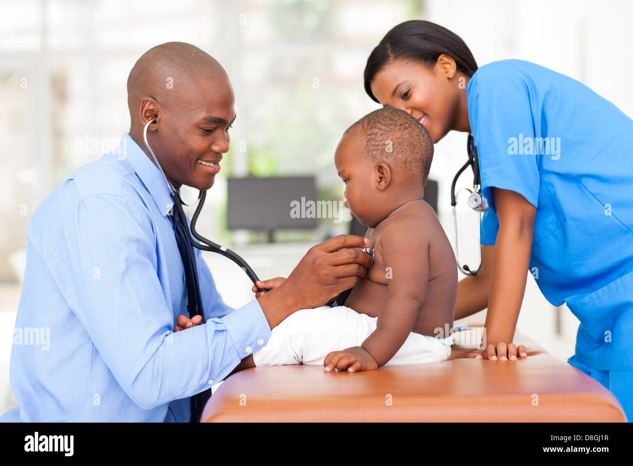 African American male pediatric doctor examining baby boy with female ...