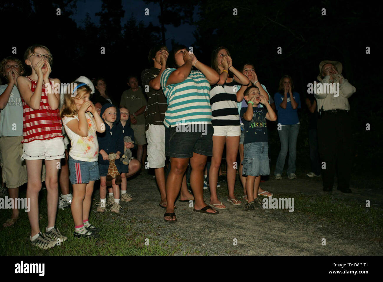 A group of children and adults are gathered together outdoors at night ...