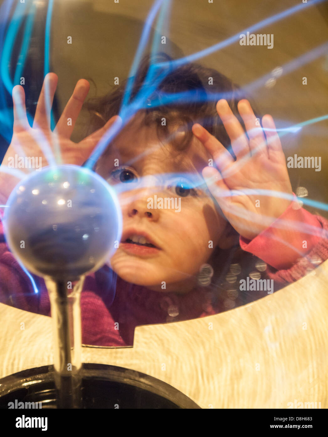 Small girl touches a plasma ball with her hands and watches the ...