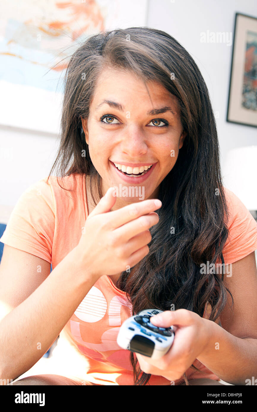 young woman with remote control laughing at something on television ...
