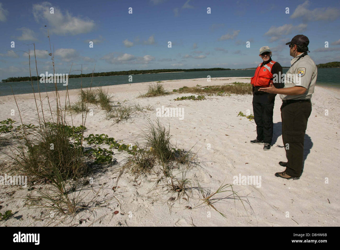 An employee on a white sand beach, interacting with a visitor wearing ...