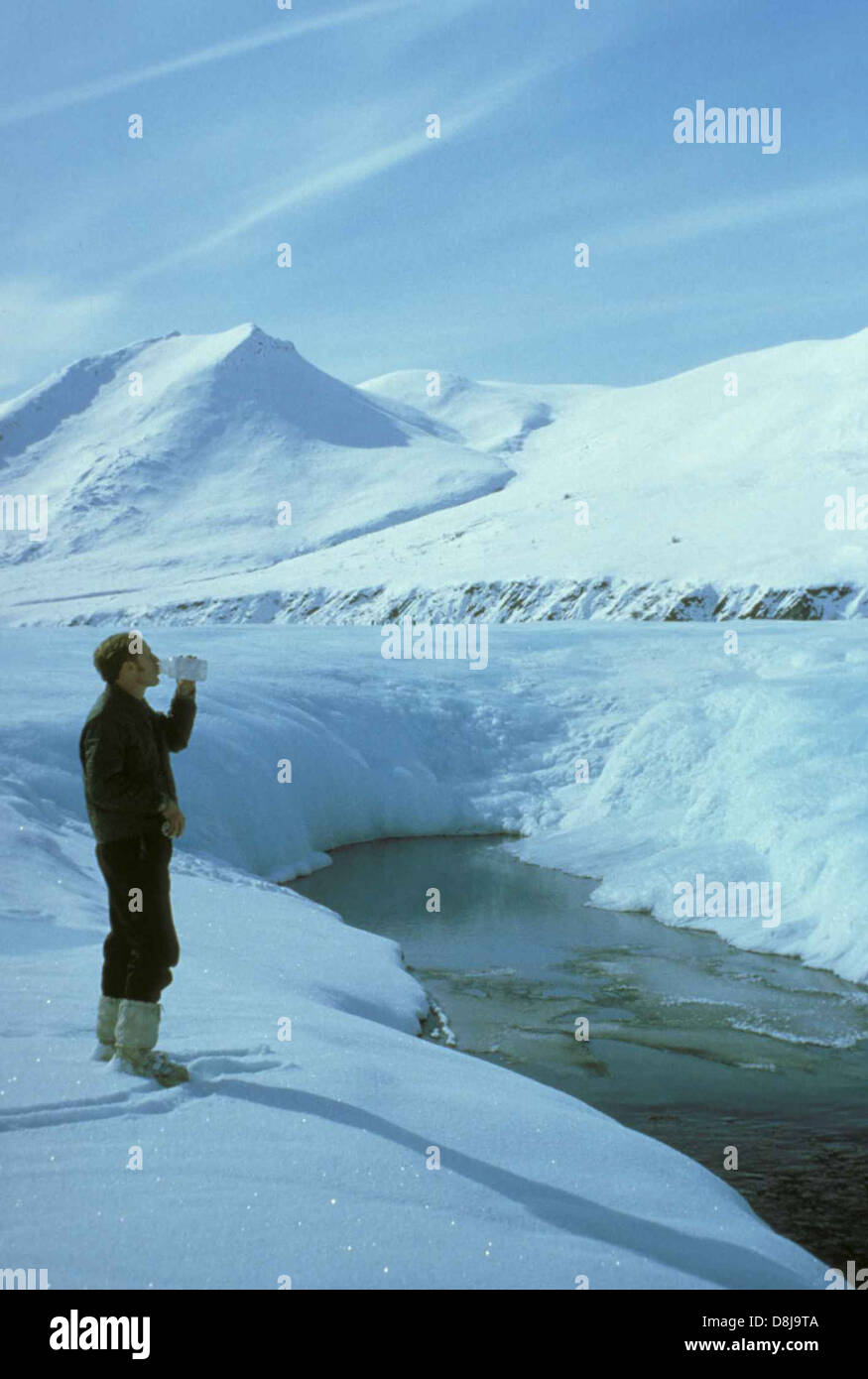 A hiker rests on a mountain trail, drinking water from a bottle. The ...