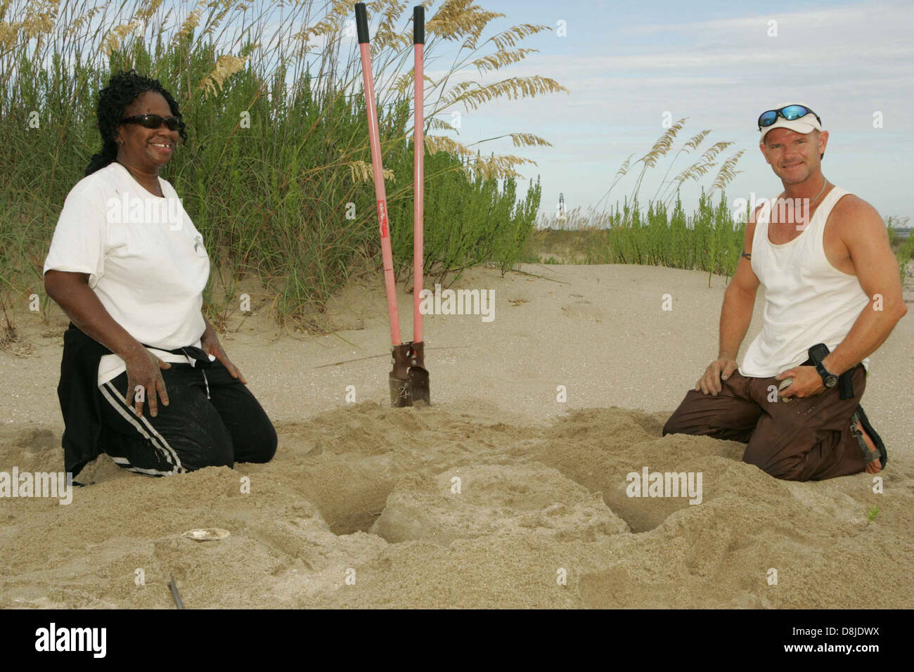A man and woman are seen digging a hole in the sand at the beach ...