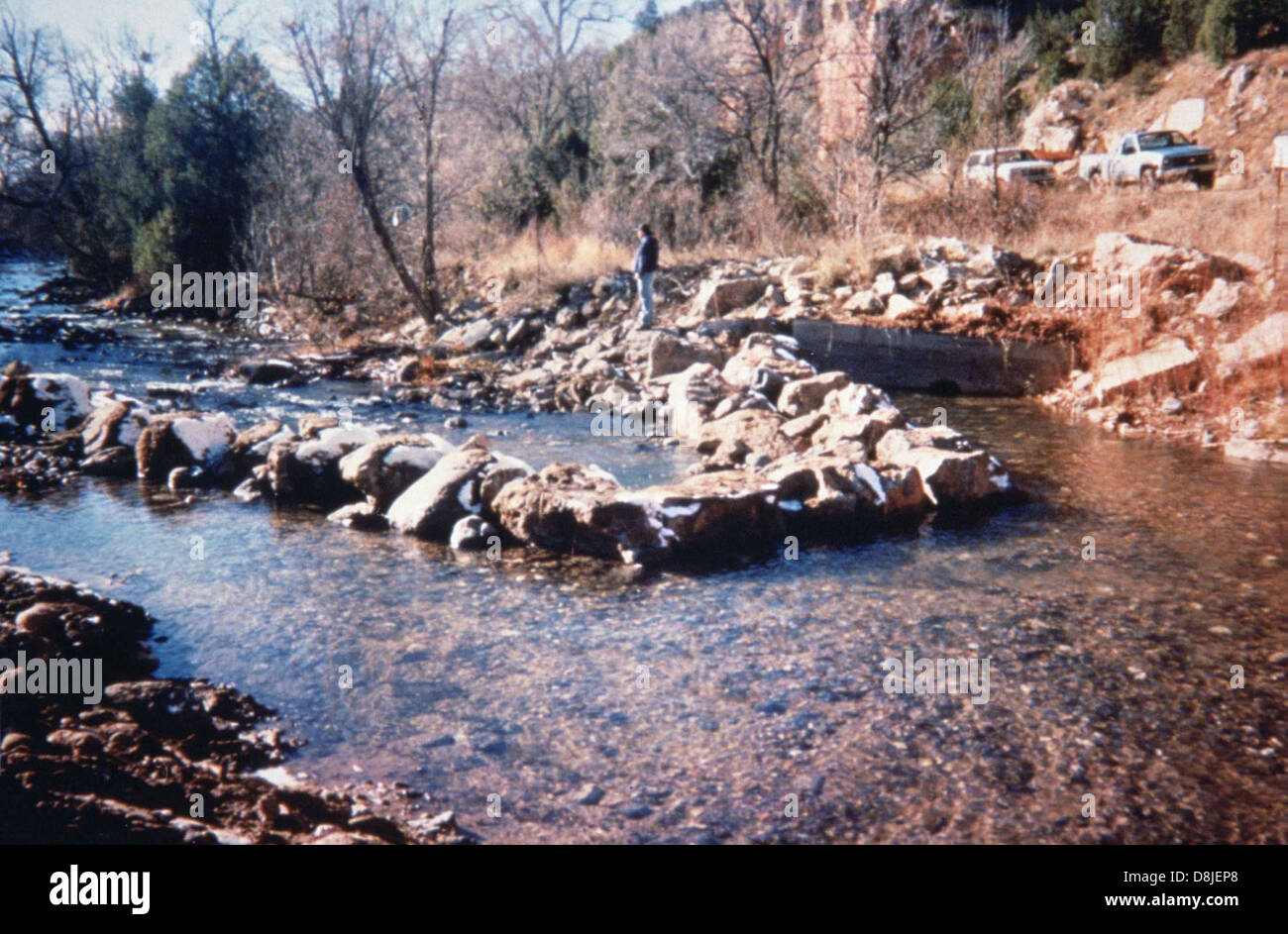 A man stands near a water diversion structure, observing the flow of ...