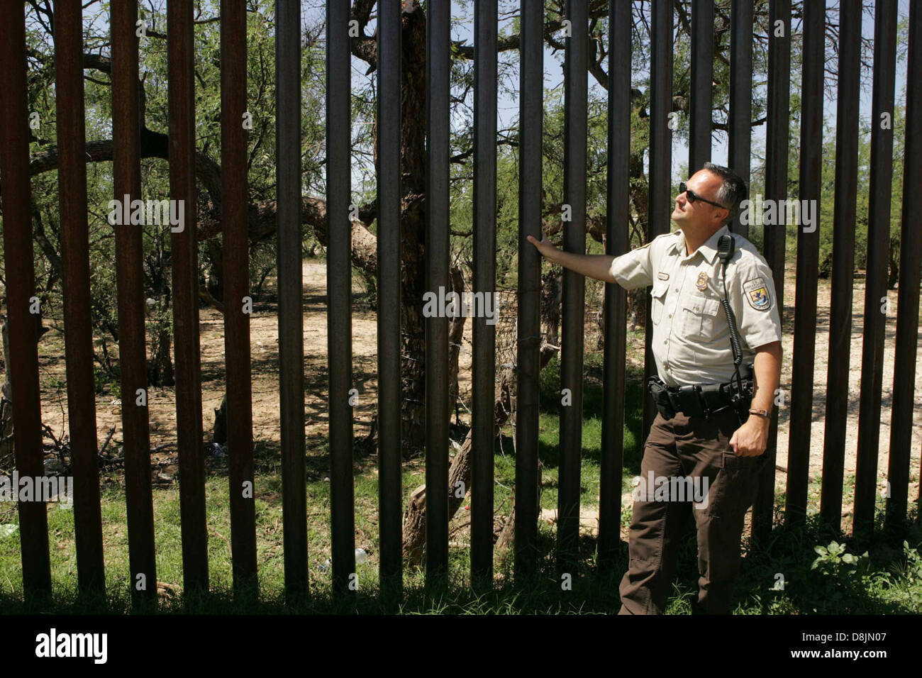 A border patrol officer stands near a border fence, wearing a uniform ...