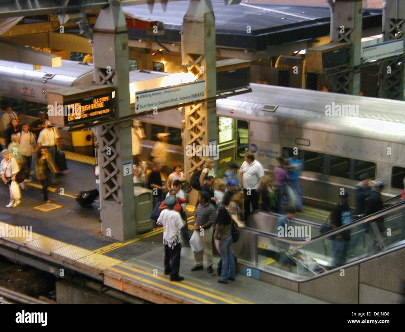 A bustling train station filled with people waiting for or boarding trains. The scene captures ...