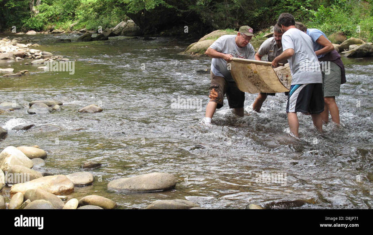 A group of people standing in shallow water, using a blanket as a ...