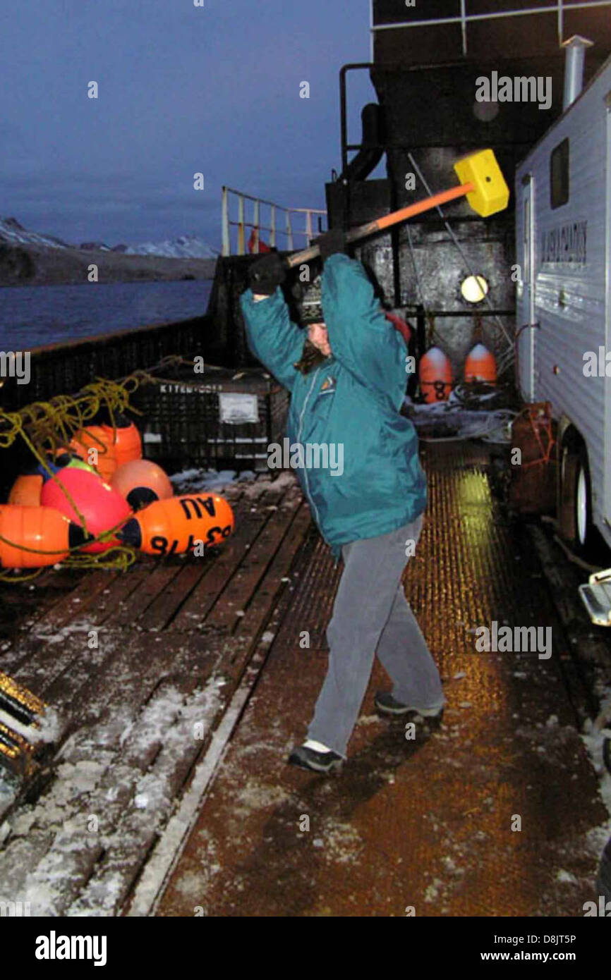 This stock photo shows a person on a ship using a tool to smash ice on ...