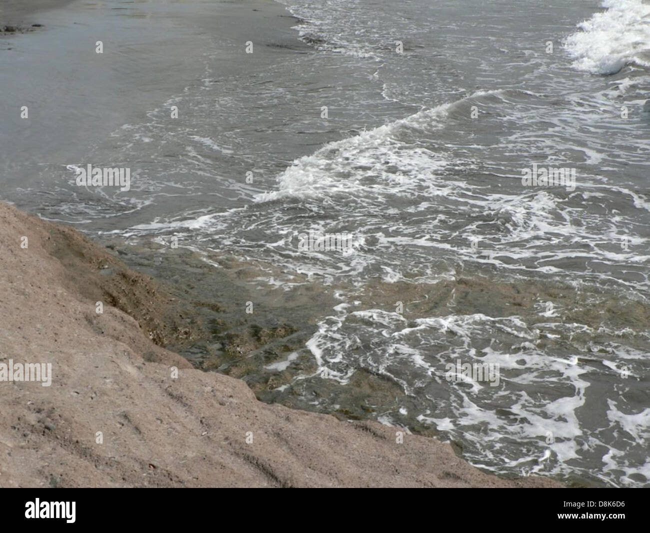 A coastal scene featuring a shoreline of brown rock and sand. The rocky ...
