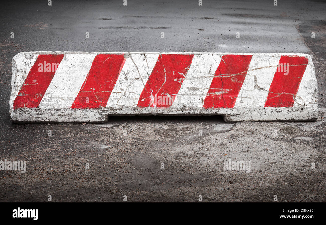 Red and white striped concrete road barrier lying on the pavement ...