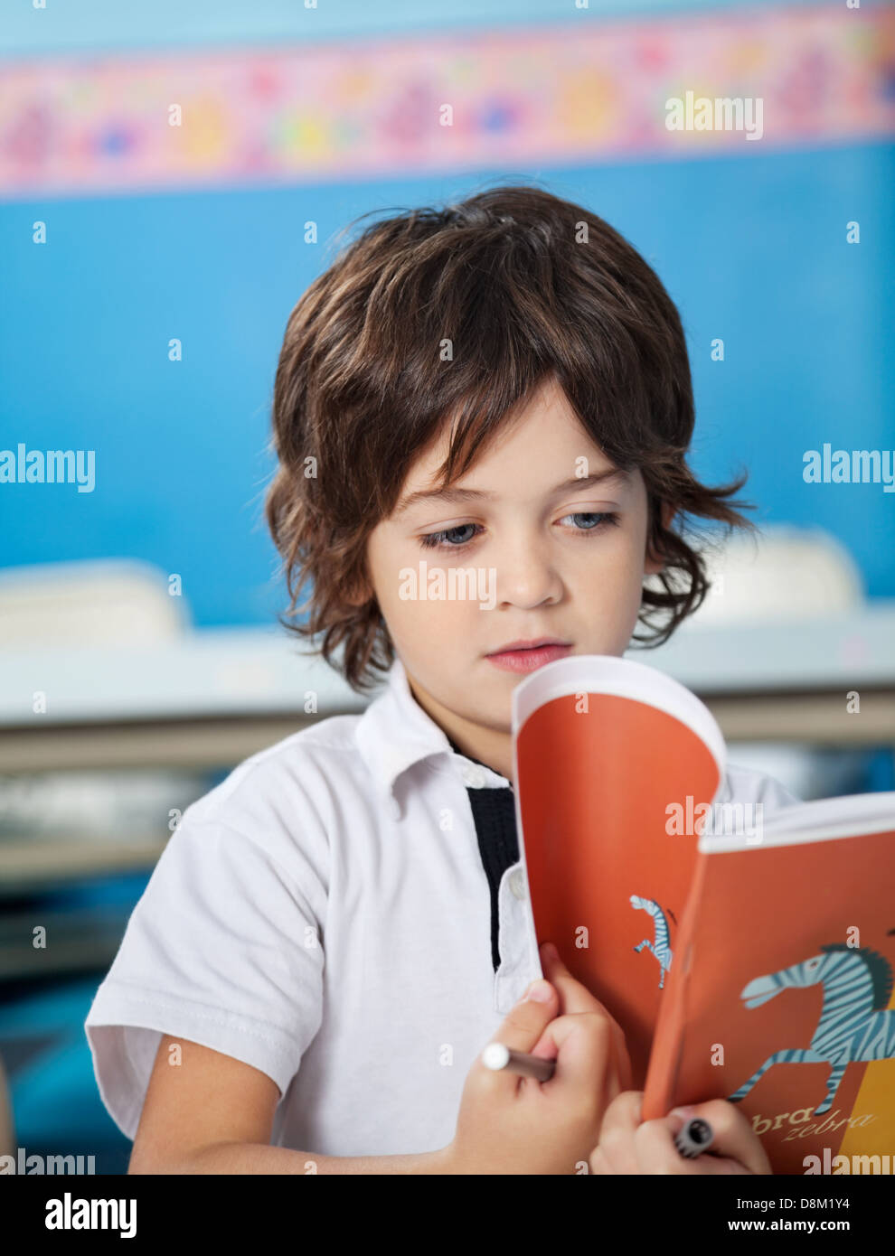 Boy Reading Book In Classroom Stock Photo - Alamy