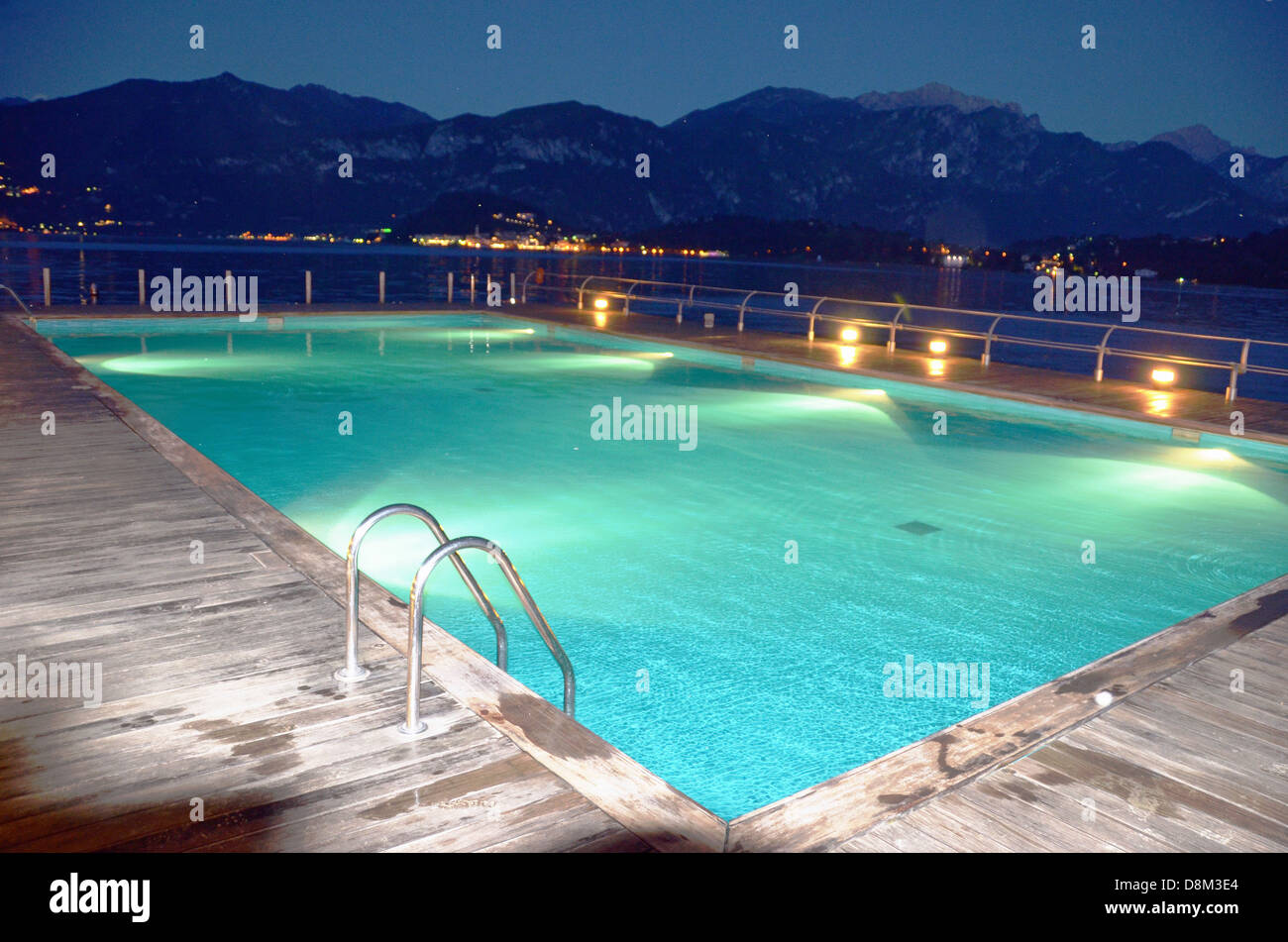 This image features a swimming pool at night, with water reflecting the ...
