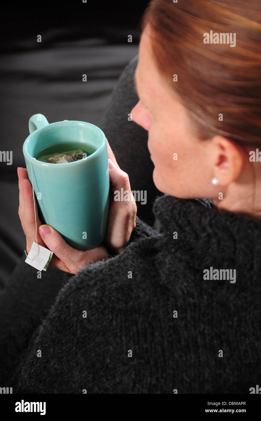 A woman holding a cup of tea while relaxing on the couch Stock Photo ...