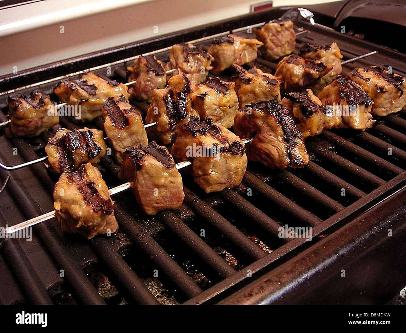 A close-up of beef meat sizzling on a grill, with visible char marks ...
