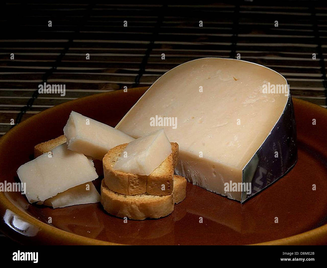 A wedge of Gouda cheese sits on a plate, illuminated under the glow of ...