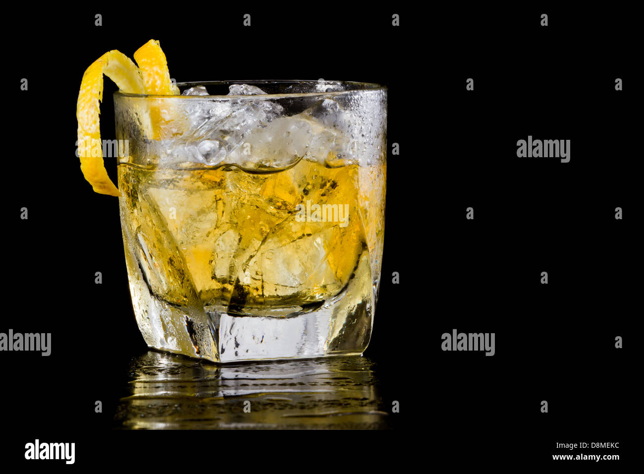 glass of whiskey over ice served on a dark bar garnished with a twist ...