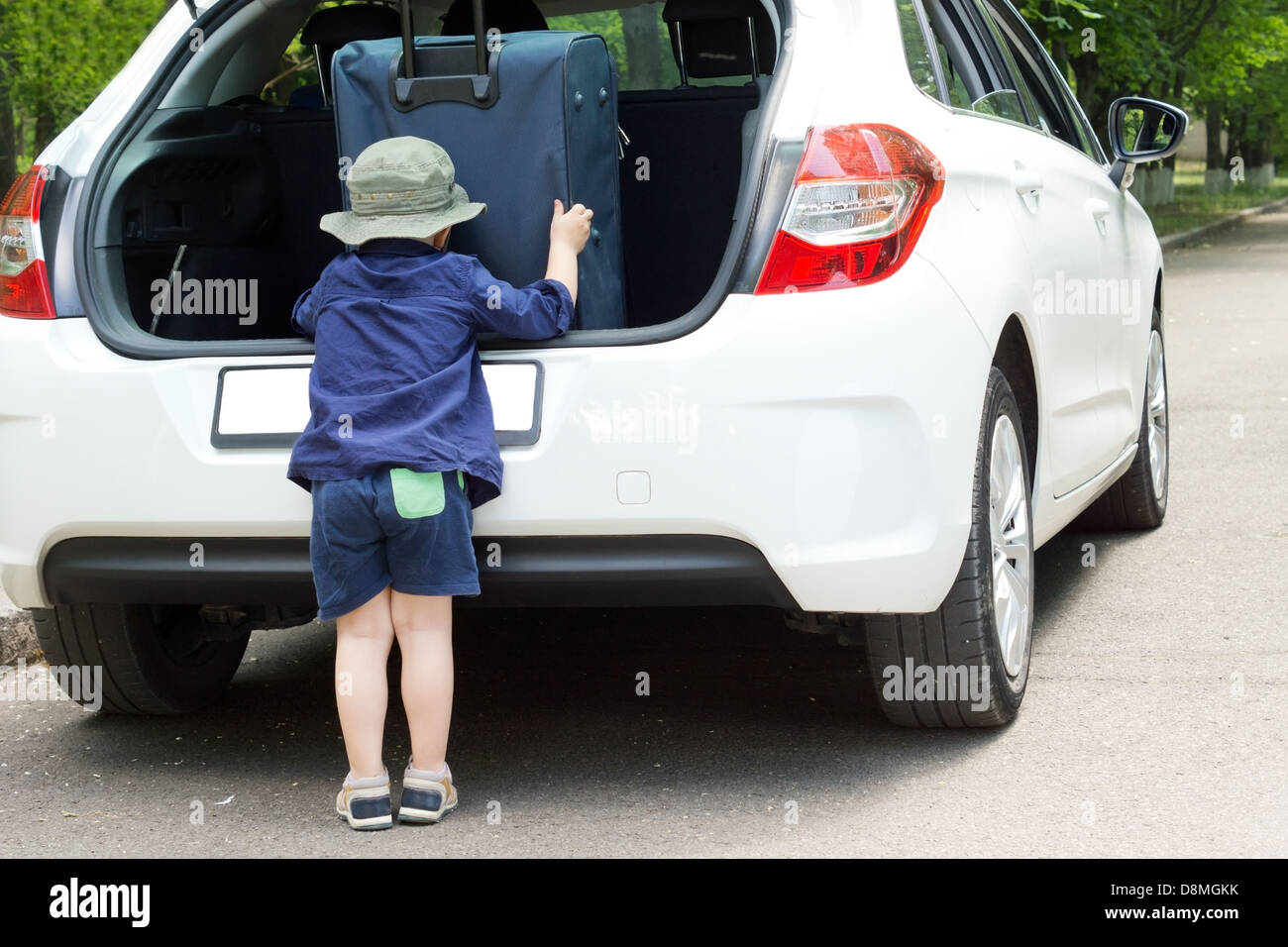 Small boy packing his luggage into the open back of a hatchback car as ...