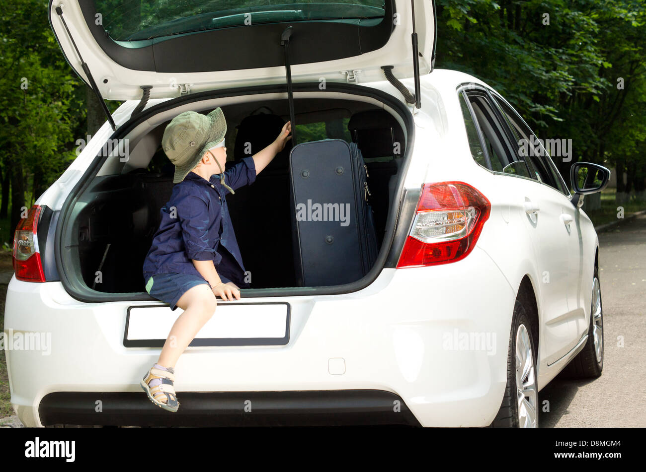 Playful boy entering in the open truck of a modern white hatchback car ...
