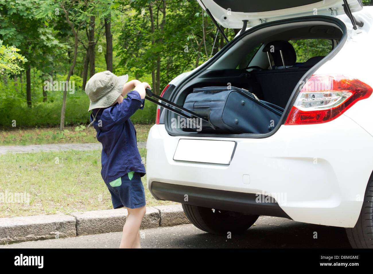 Small boy struggling to load his suitcase into the open back of a ...