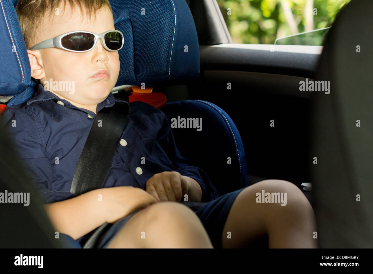 Tired young boy sleeping in the child car-seat in the back of a car ...