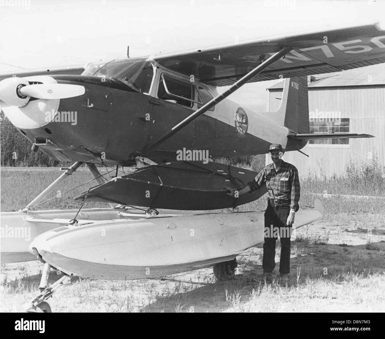 A historical photo showing a man standing next to a float plane on the ...