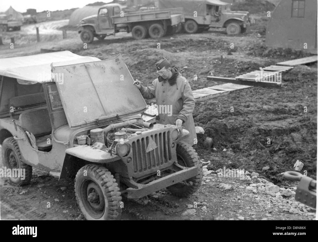 A man inspects the engine of an old World War II-era Jeep, focusing on ...