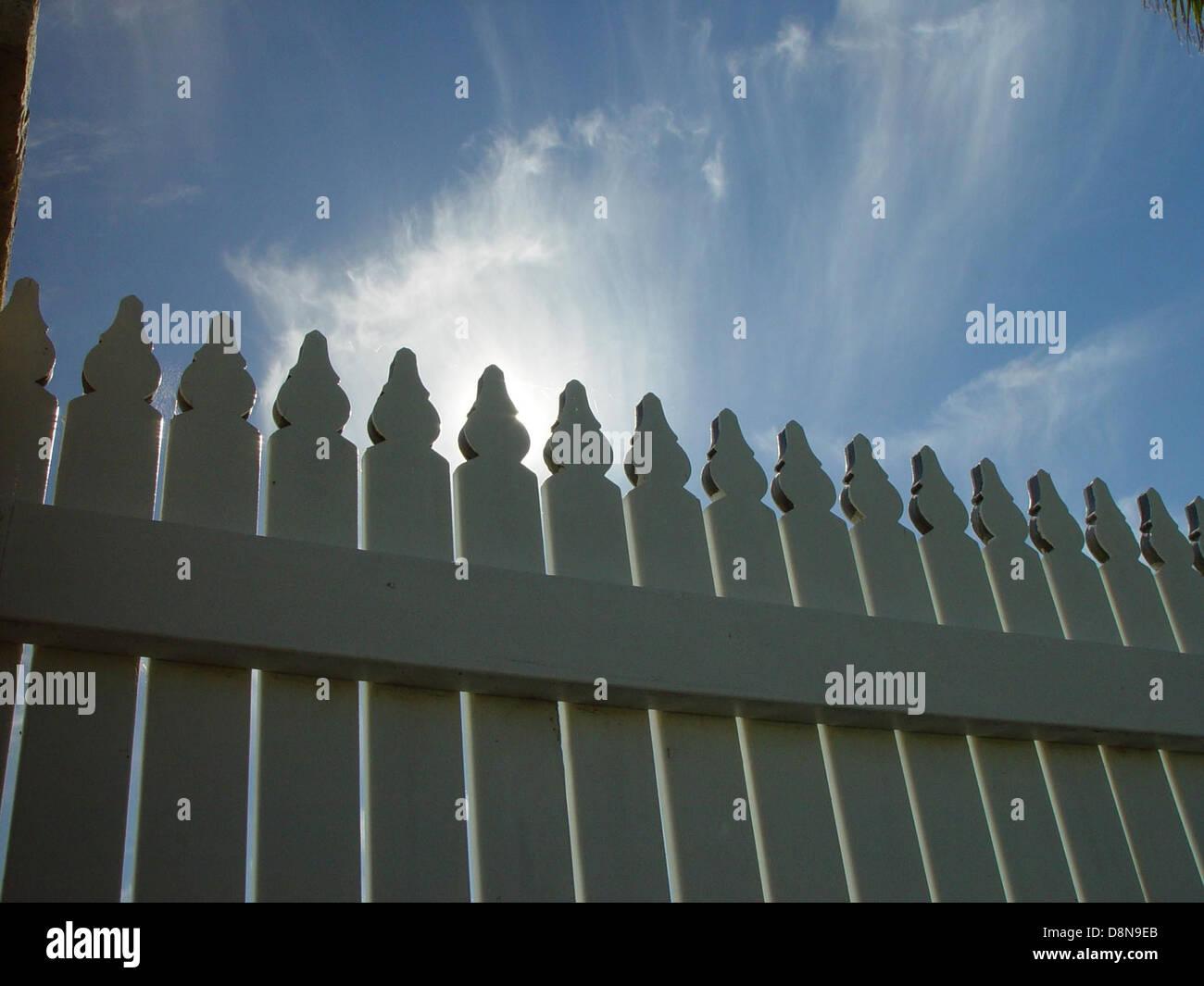 Sunlight shining over a white picket fence, casting long shadows across ...