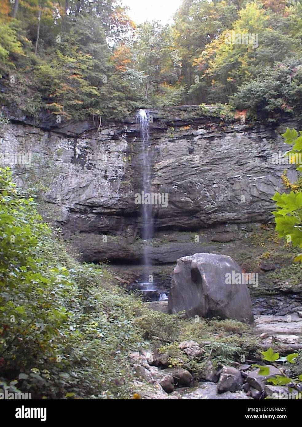 A tall waterfall cascades over a rocky cliff, surrounded by lush ...