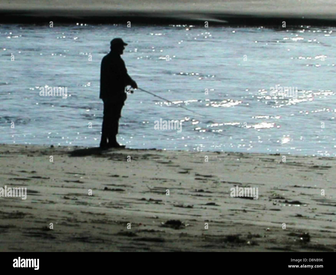 The silhouette of a sport fisherman stands at the riverbank, casting a ...