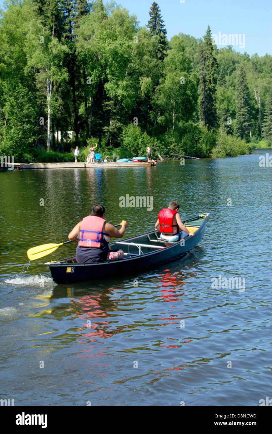 Two people paddle a canoe on a tranquil lake, with swimmers visible on ...