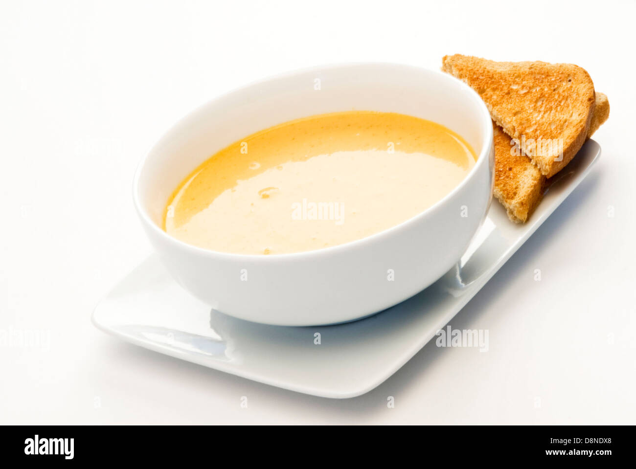 A bowl of tomato soup and toast is seen against a white background ...