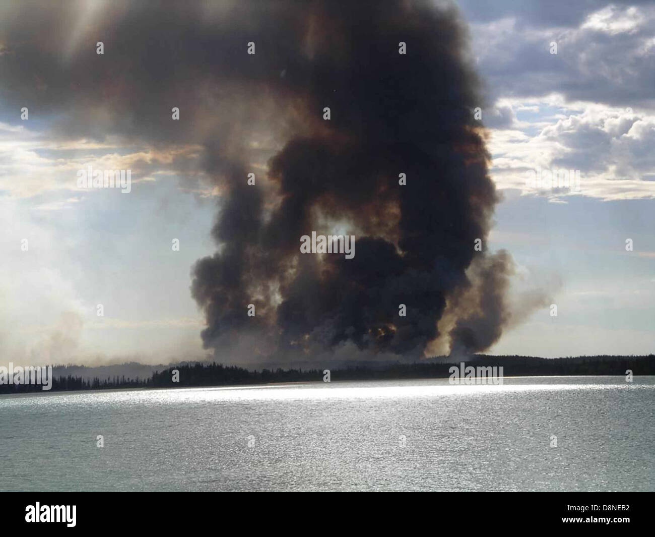 A dramatic image of thick black smoke rising from a large forest fire ...