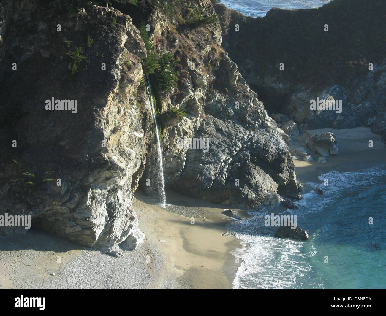 A waterfall cascading from a rocky cliff directly into the ocean ...