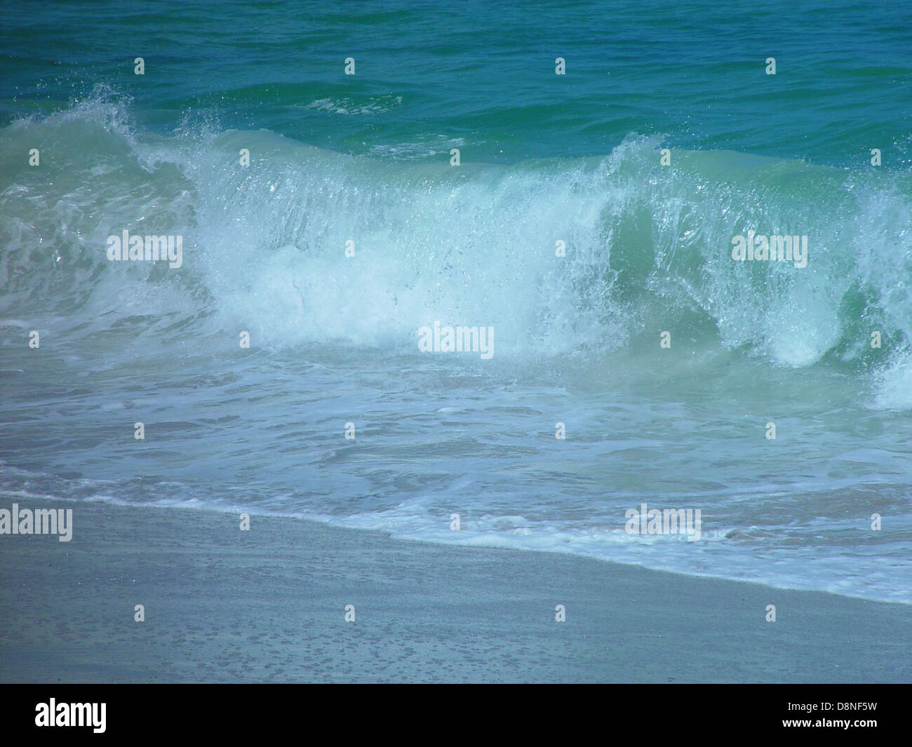A powerful wave breaks at the shore of a beach, creating a dramatic ...