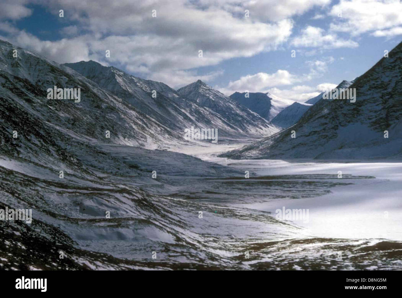 White clouds float above a snow-covered, frozen mountain range. This ...