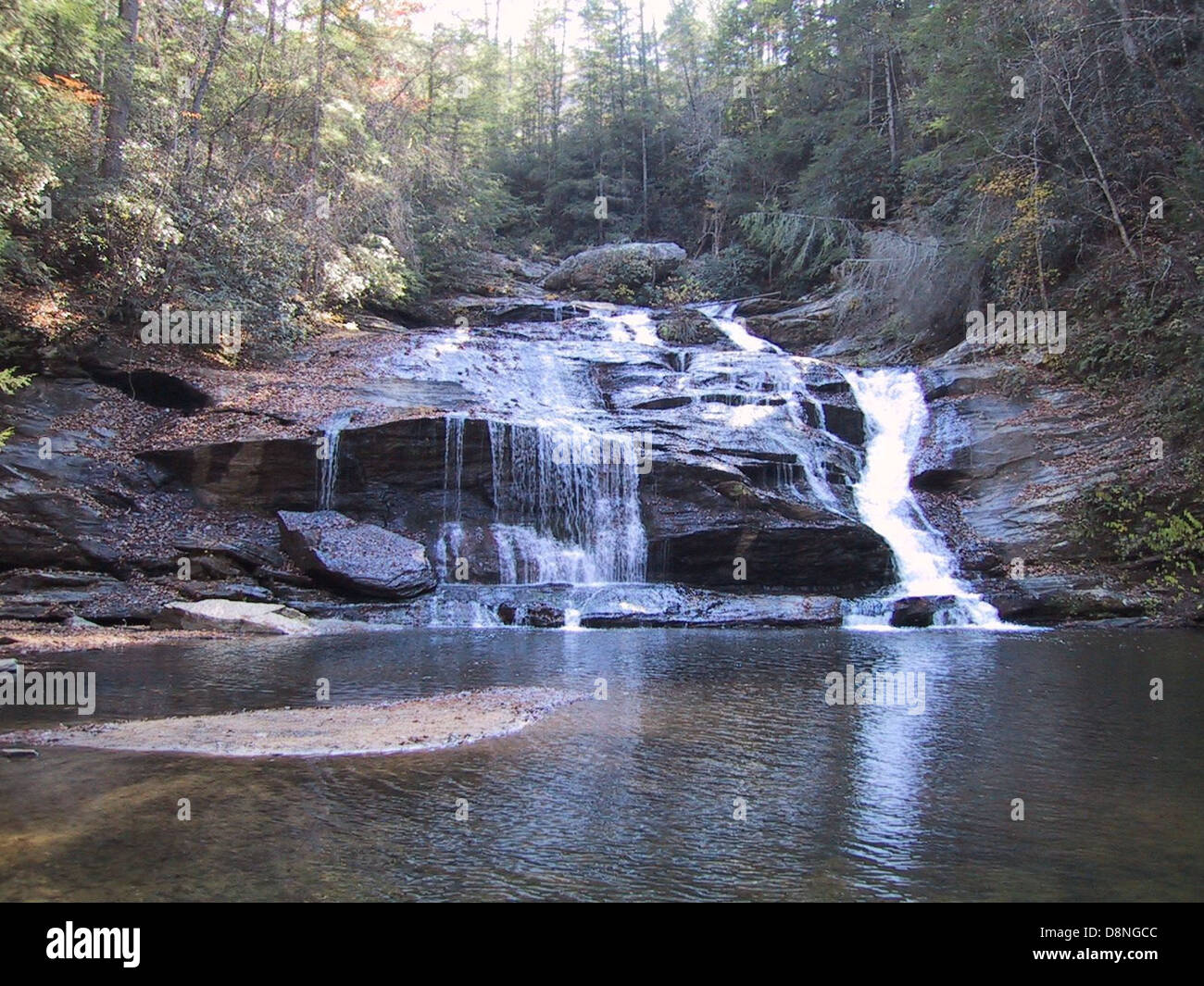 A wide waterfall cascades down into a shallow pool below. The natural ...